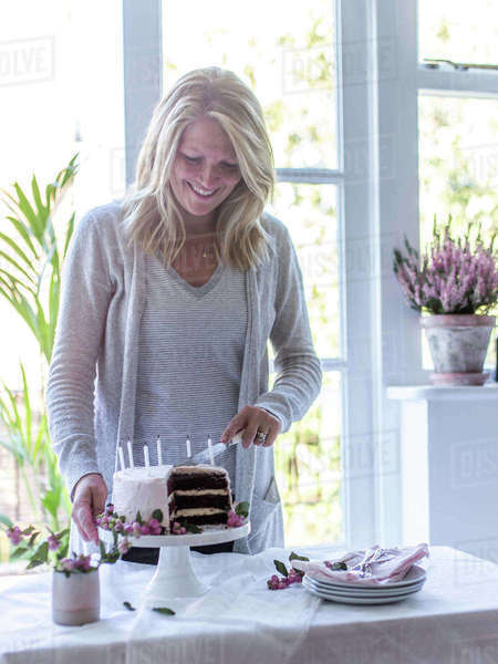 Woman slicing a chocolate birthday cake with rose water frosting ...