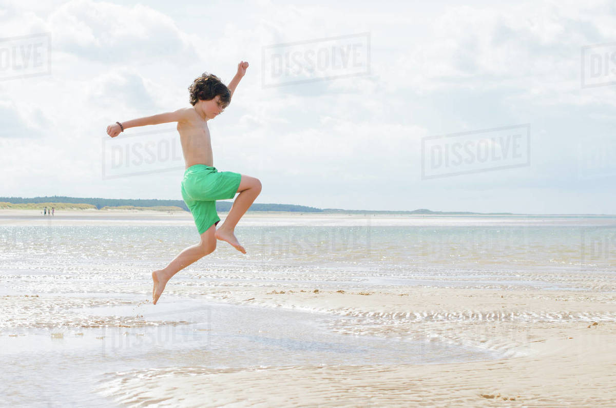 Boy on beach jumping over a tide pool - Stock Photo - Dissolve