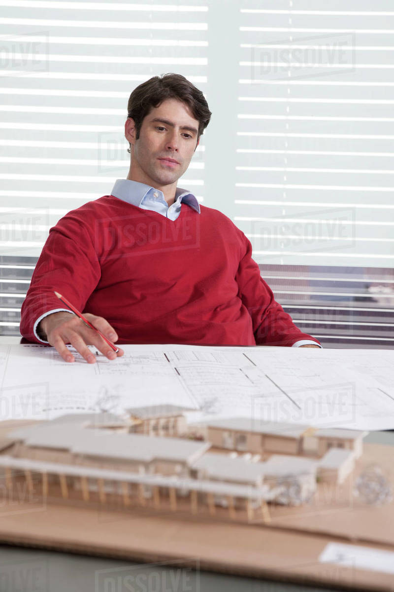 Architect at desk looking at plans and building model - Royalty-free ...