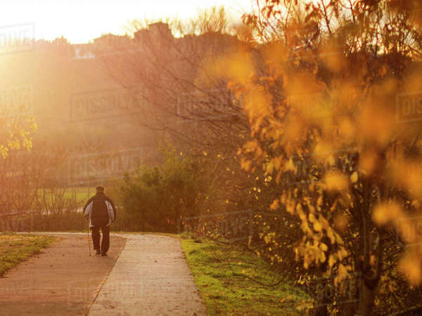 Senior man walking down road at sunset - Stock Photo - Dissolve