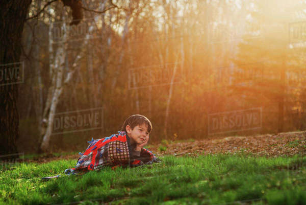 Boy lying on the grass wrapped in a blanket in the sun - Royalty-free ...