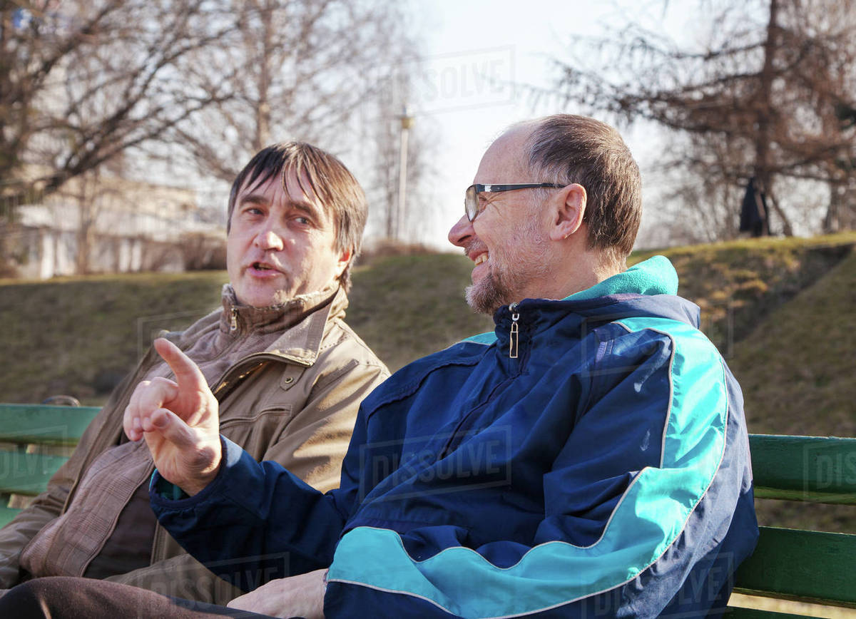 Two men sitting on a park bench talking - Stock Photo - Dissolve