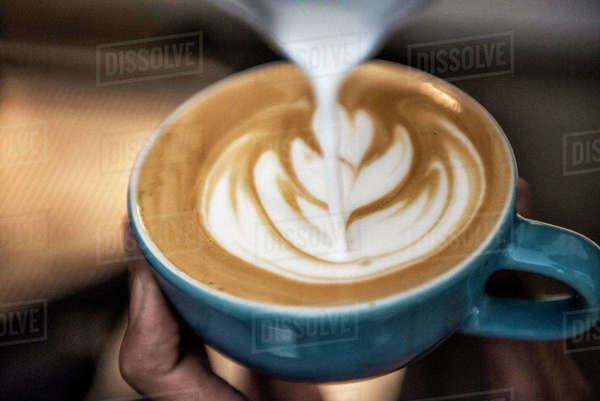 Close-up of a person pouring microfoam on a cup of coffee to make a ...