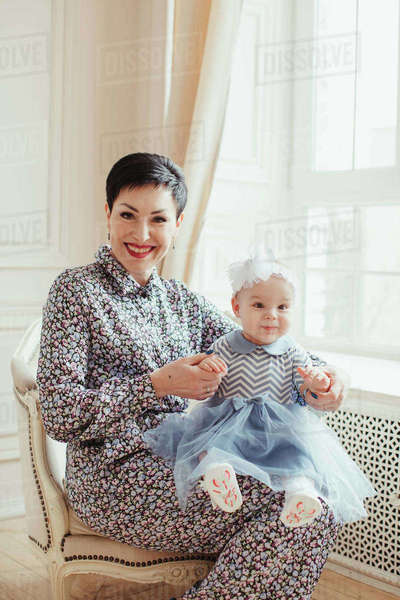 Portrait of a smiling baby girl sitting on her grandmother's lap ...