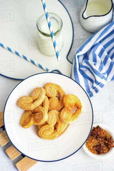 Overhead view of a bowl of palmier biscuits with a bottle of milk ...