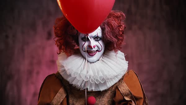 Creepy clown releases a red ball and shows his face. Clown in a ...