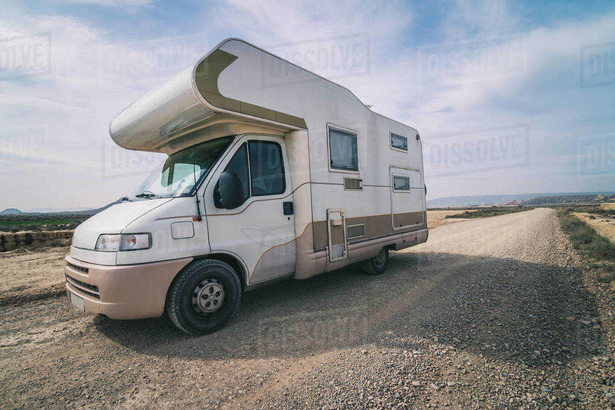 Side view of white camper standing on empty road along semi-desert with ...