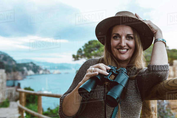 Adult woman observing view with binocular while standing at fence on ...