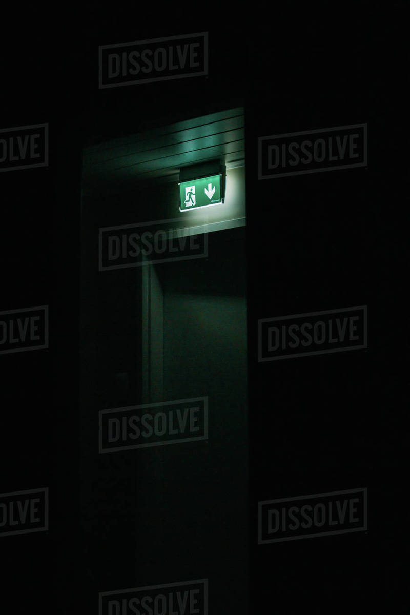 Green exit sign shining over closed door in dark room - Royalty-free ...