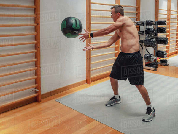 Powerful shirtless male throwing heavy ball against wall during fitness ...