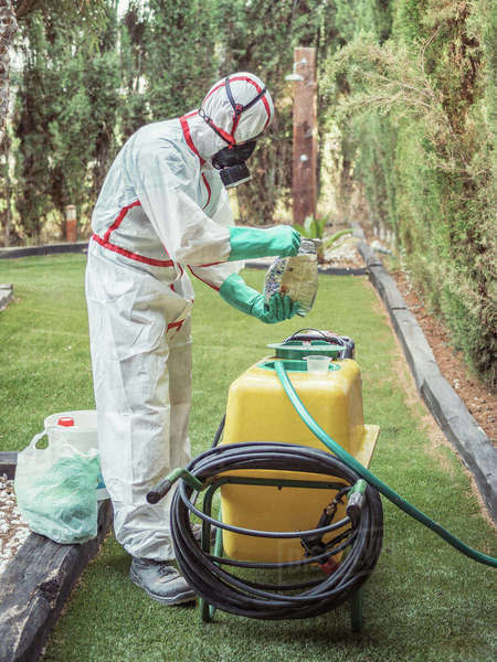 Side view of fumigator in white uniform and respiratory mask holding ...