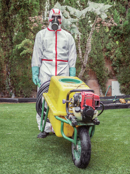 Specialist in uniform for fumigation holding yellow trolley in yard ...