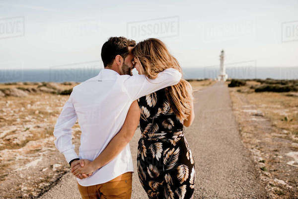 Back view of tender couple hugging on asphalt road to lighthouse and ...