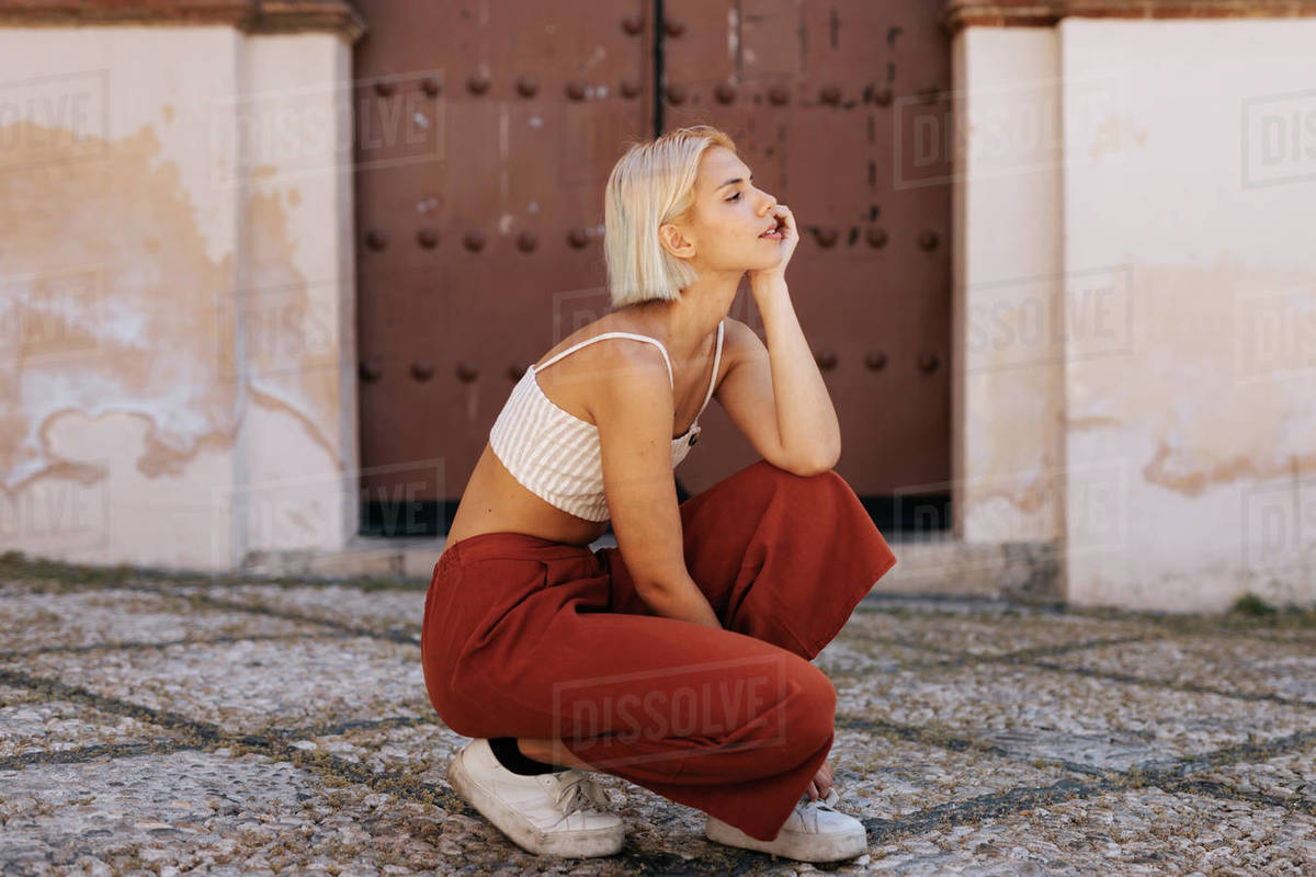 Attractive young woman in stylish outfit crouching looking away against ...