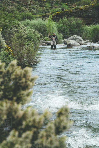 Equipped man harling fish while standing inside water in river stream ...