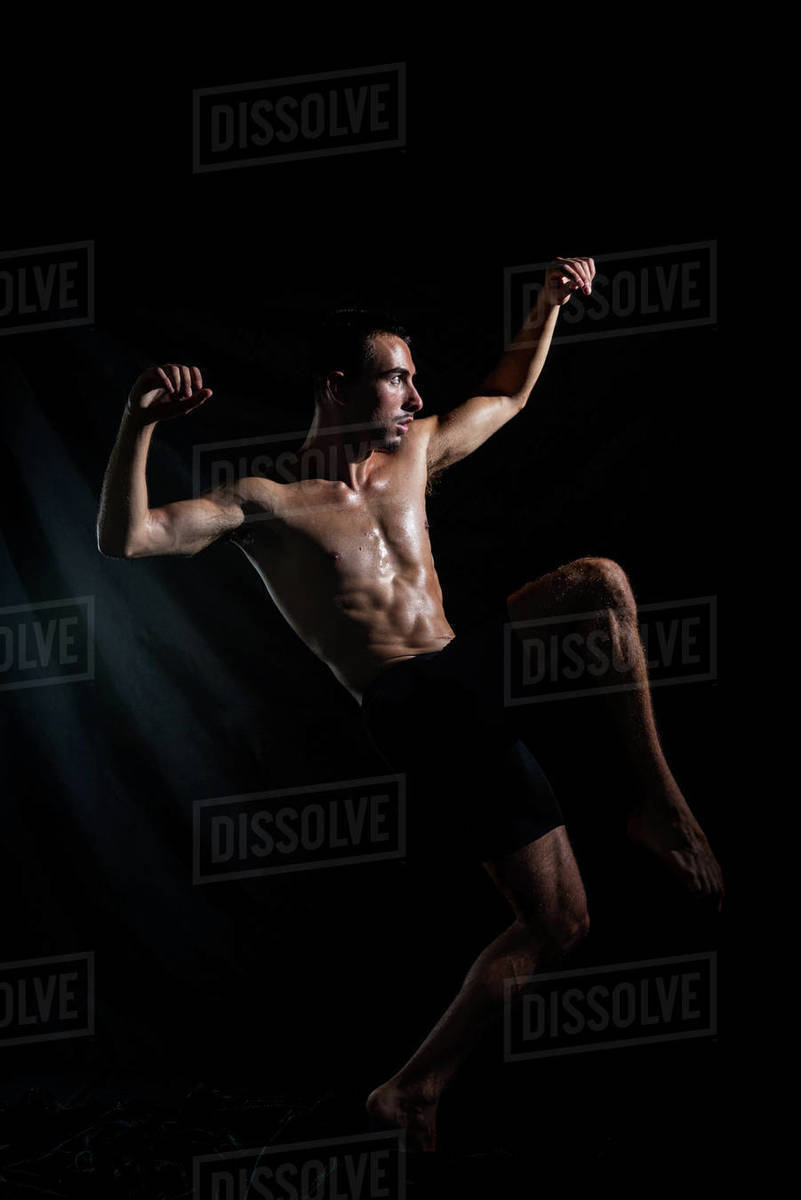 Full body of faceless tanned sporty shirtless dancer in shorts raising ...