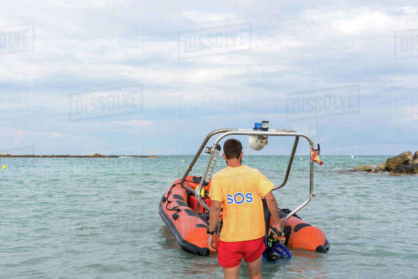 Back view of unrecognizable lifeguard in standing near modern motorboat ...
