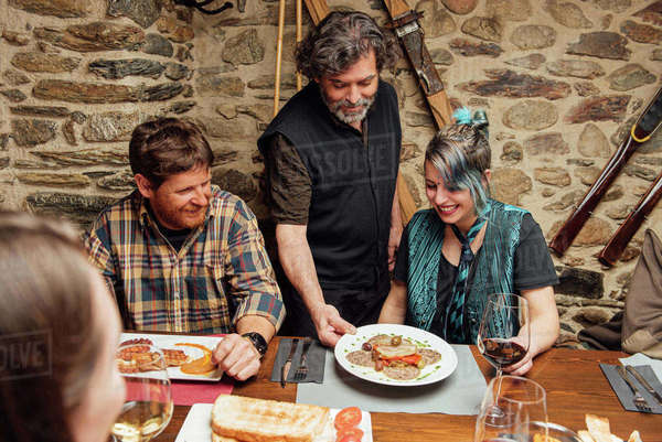 Male standing at wooden table in cafe with group of friends and ...