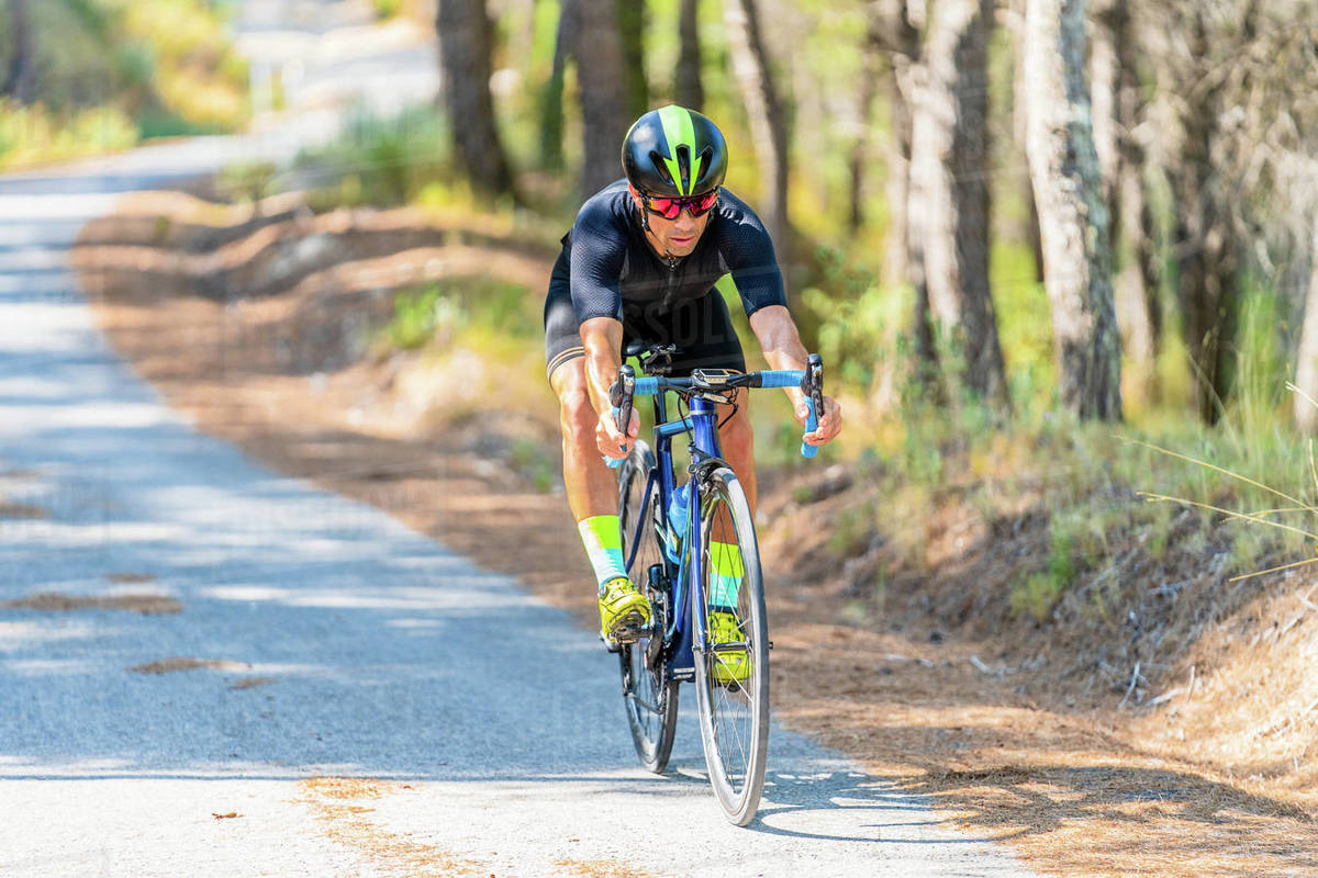 Full length of strong male bicyclist riding bike on curvy paved road ...