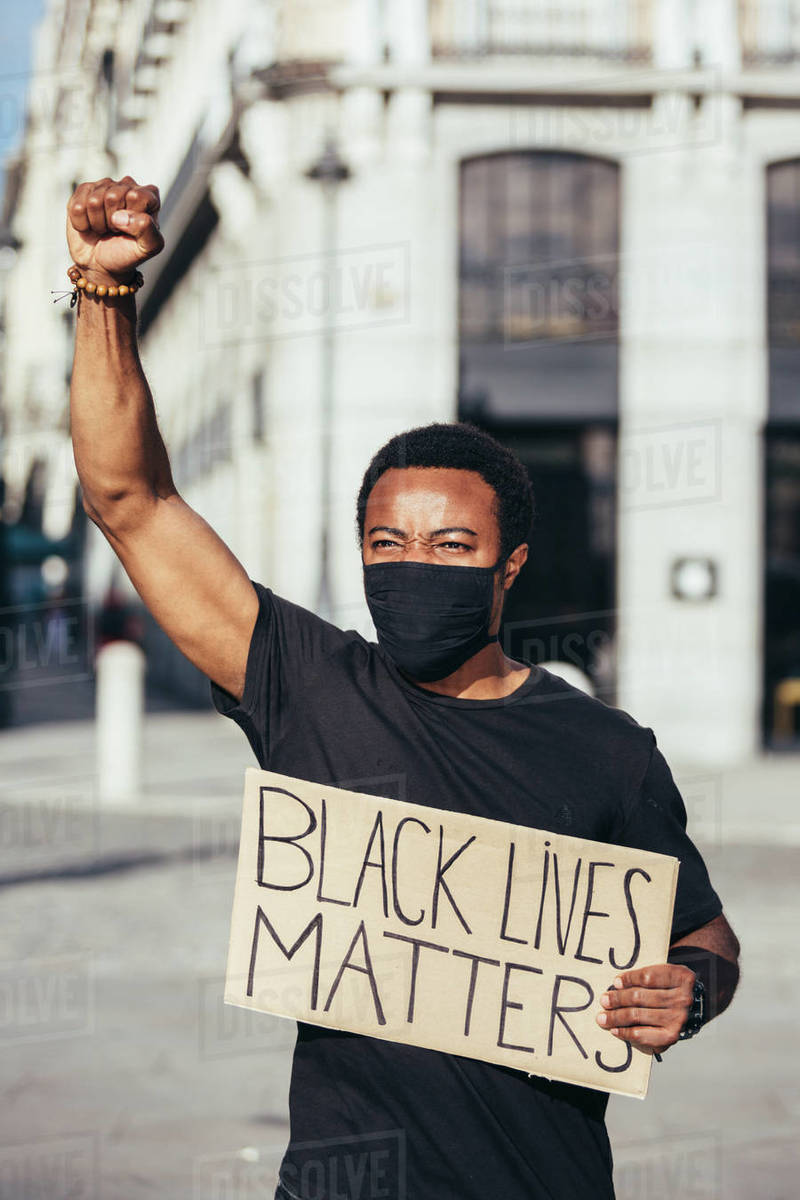 Man protesting at a rally for racial equality holding a poster against ...