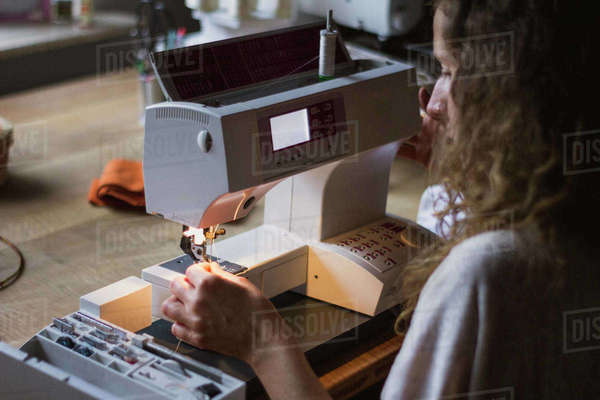 Back view of anonymous crop woman using sewing machine making clothes ...