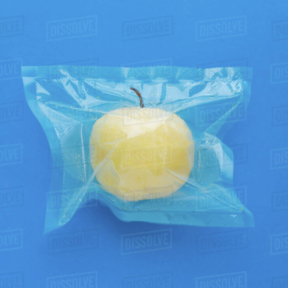 Top view of ripe yellow peeled apple in vacuum plastic bag on blue ...