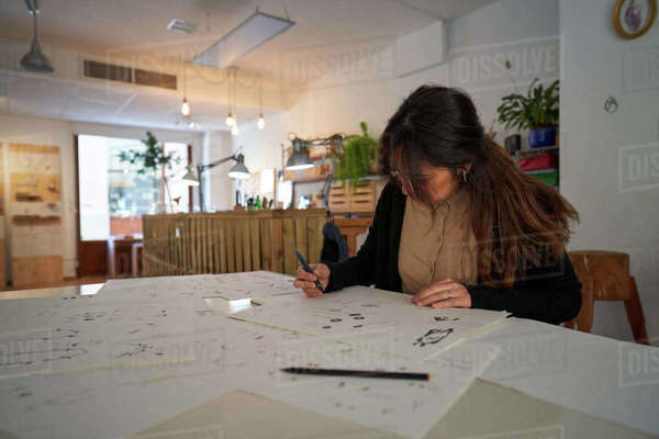 Woman sitting at a table with a pencil drawing jewels on paper - Stock ...