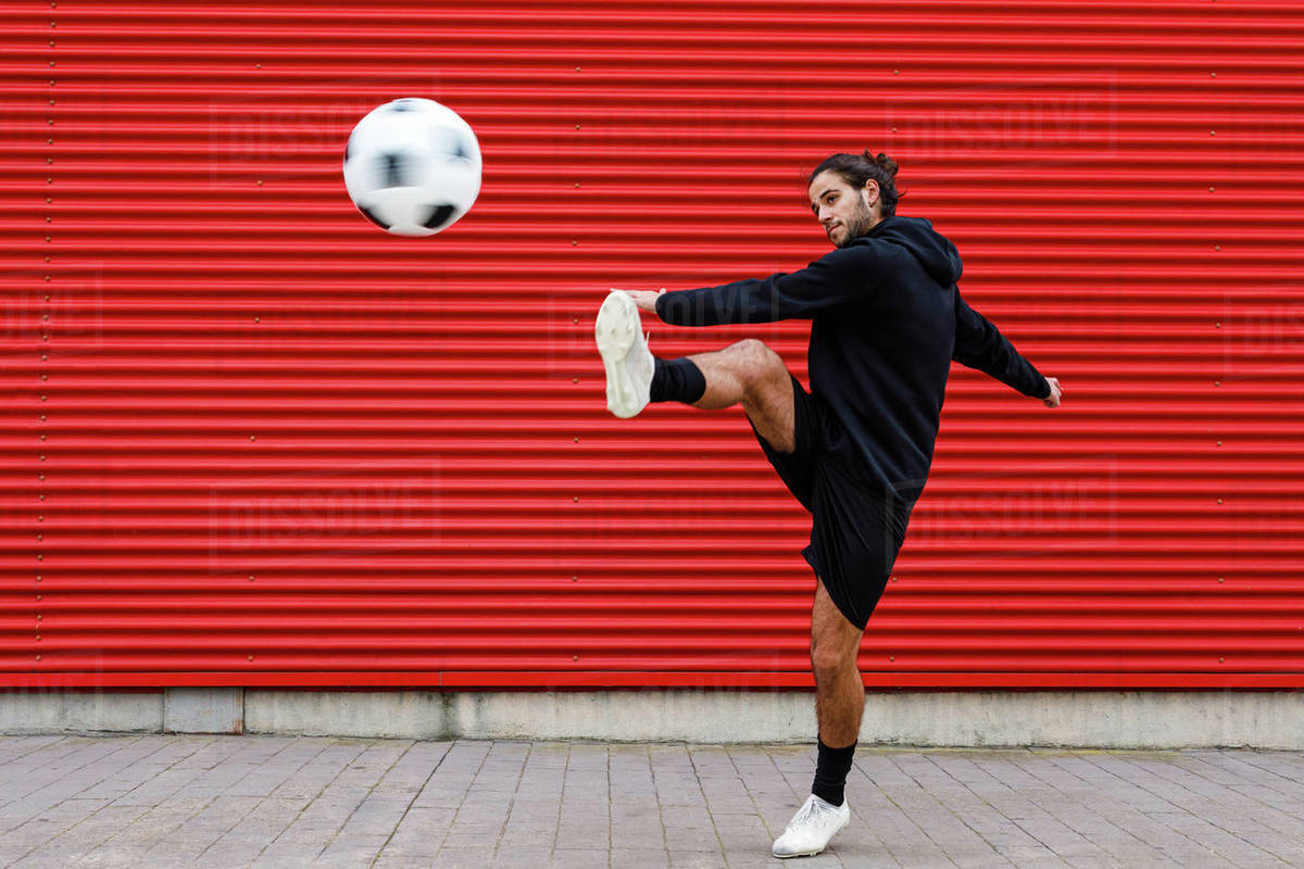 Man playing soccer ball on street - Stock Photo - Dissolve