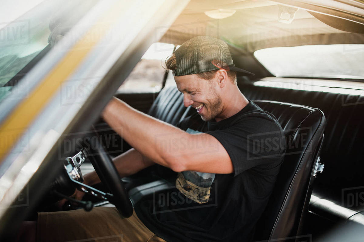 Cheerful young man sitting in car and starting engine Horizontal ...