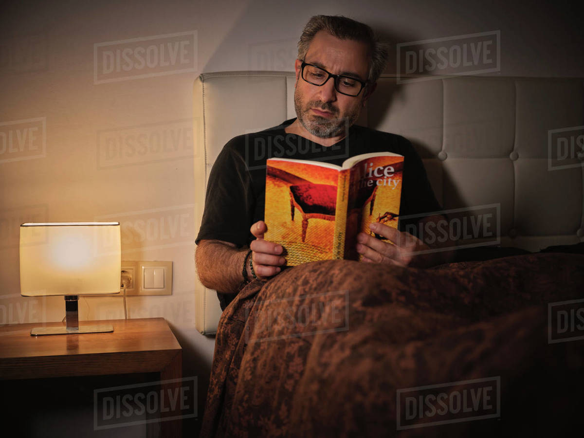 Relaxed man in bed reading a book before sleeping and resting - Stock ...