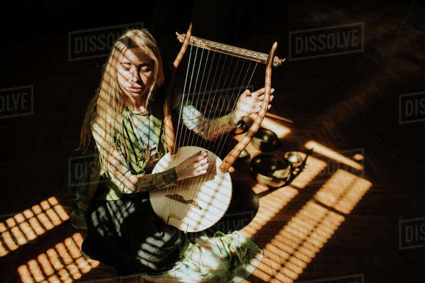 Lady playing lyre in dark room - Stock Photo - Dissolve