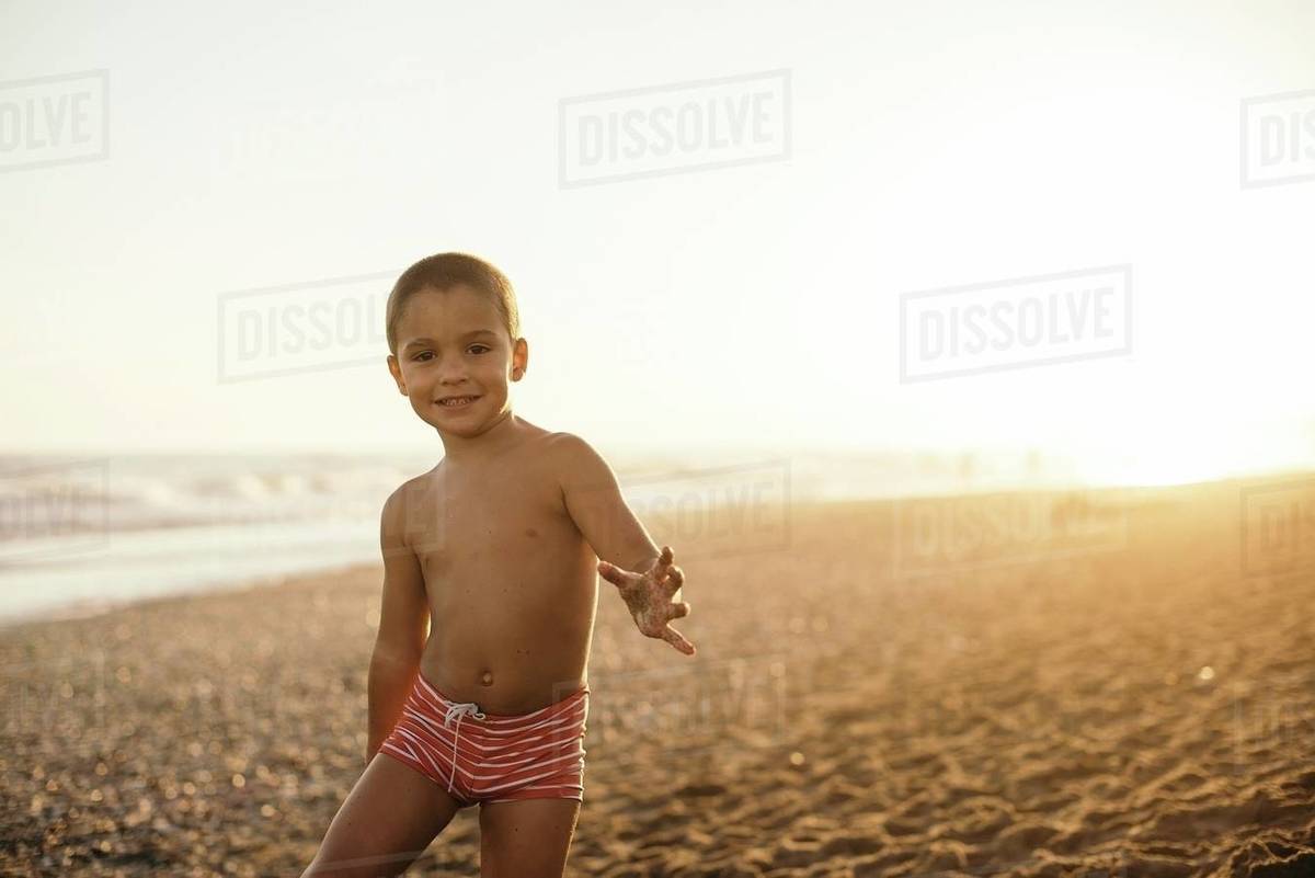 Happy shirtless boy smiling and looking at camera while standing on ...