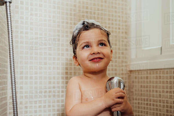 Smiling little child with foam on head standing in bathroom with shower ...
