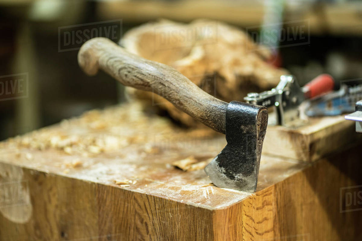 Shabby axe with wooden handle sticking out of large square wooden table ...