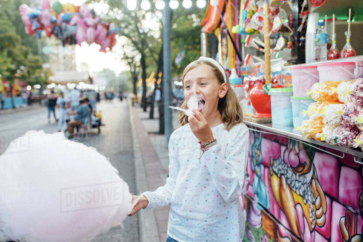 Cheerful girl eating cotton candy on street - Stock Photo - Dissolve