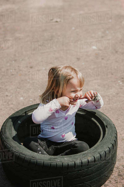 From above of happy adorable little girl sitting inside car tire while ...