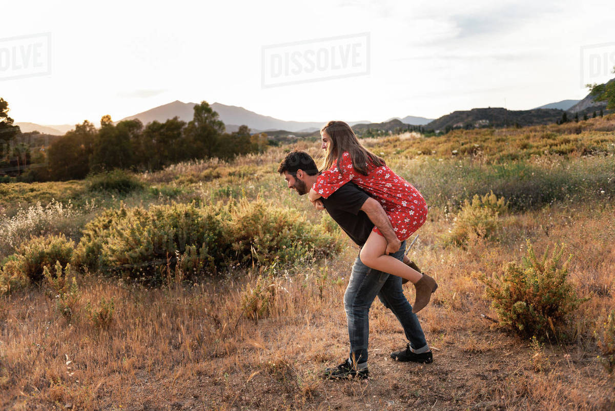 Side view of cheerful couple playing piggyback while standing among ...