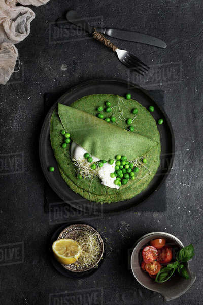 Overhead still life of pea crepes served on a dark dish placed on dark ...