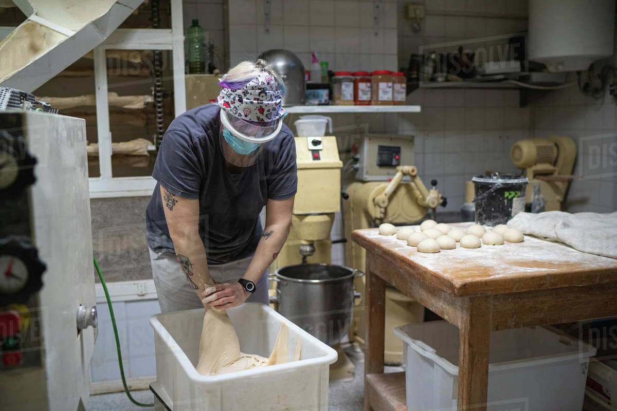 Unrecognizable female baker in mask working in bakery and kneading raw ...