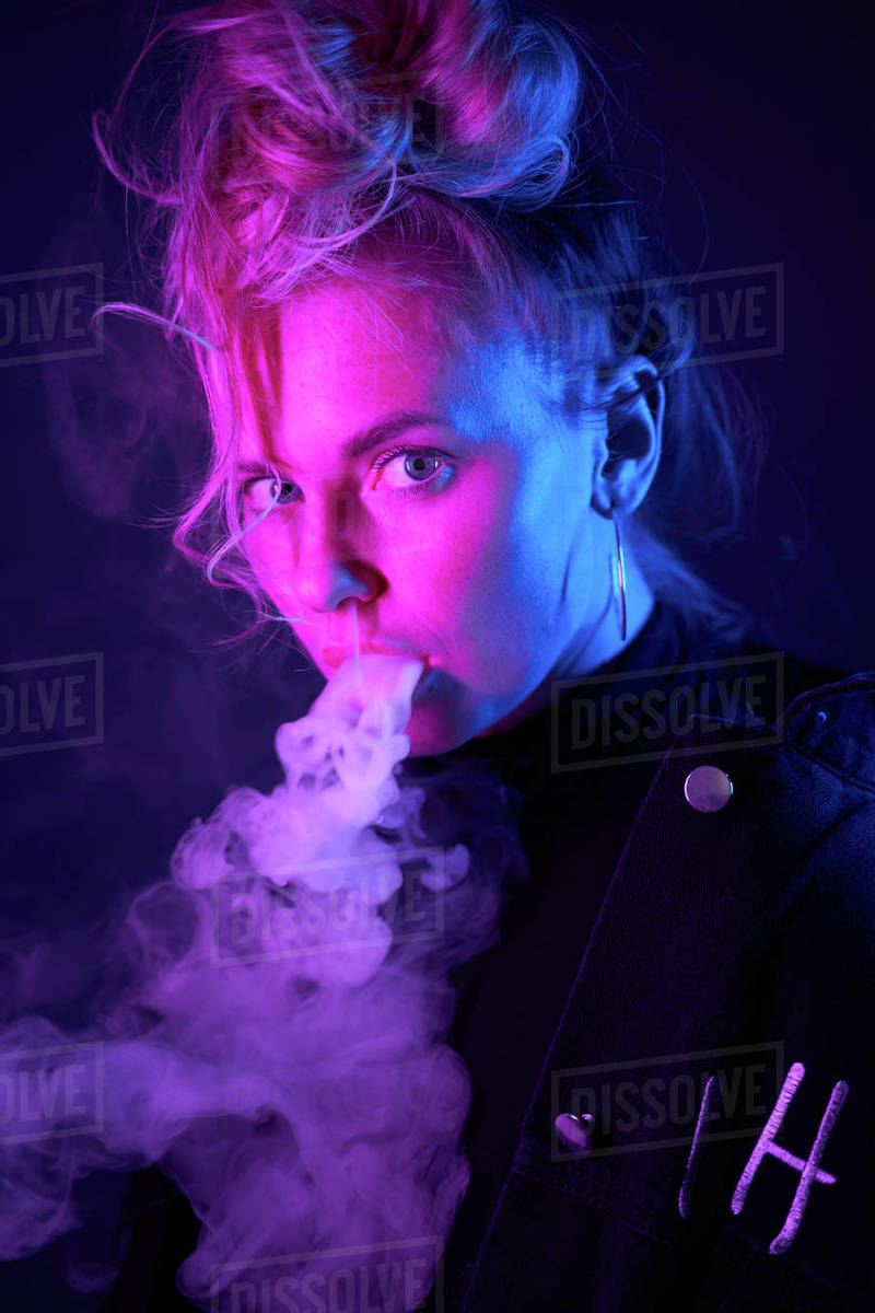 Side view of young cool female smoking vape in neon light in dark ...