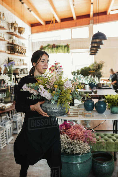 Professional female florist in black uniform carrying ceramic pot with ...
