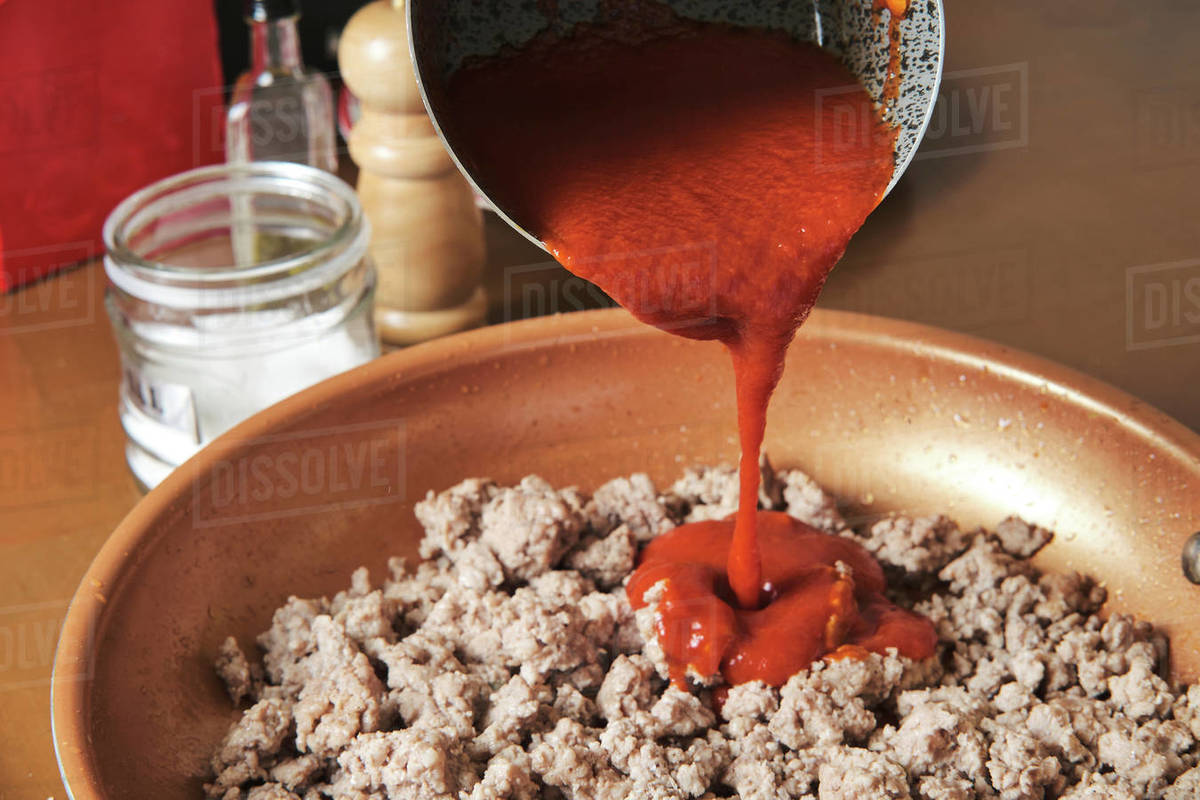 Anonymous person pouring homemade tomato sauce into frying pan with ...