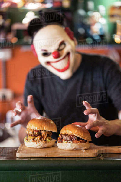 Male chef wearing scary clown mask standing at counter with delicious ...