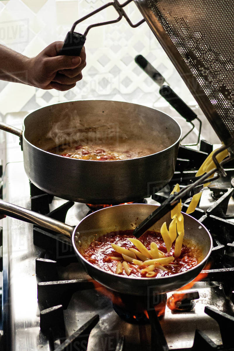 Unrecognizable cook spilling boiled pasta into frying pan with tomato ...