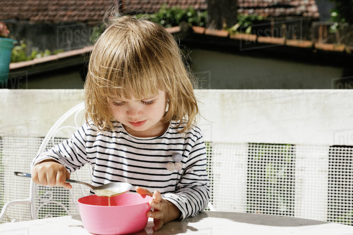 Adorable little child sitting at table eating from a pink bowl on ...