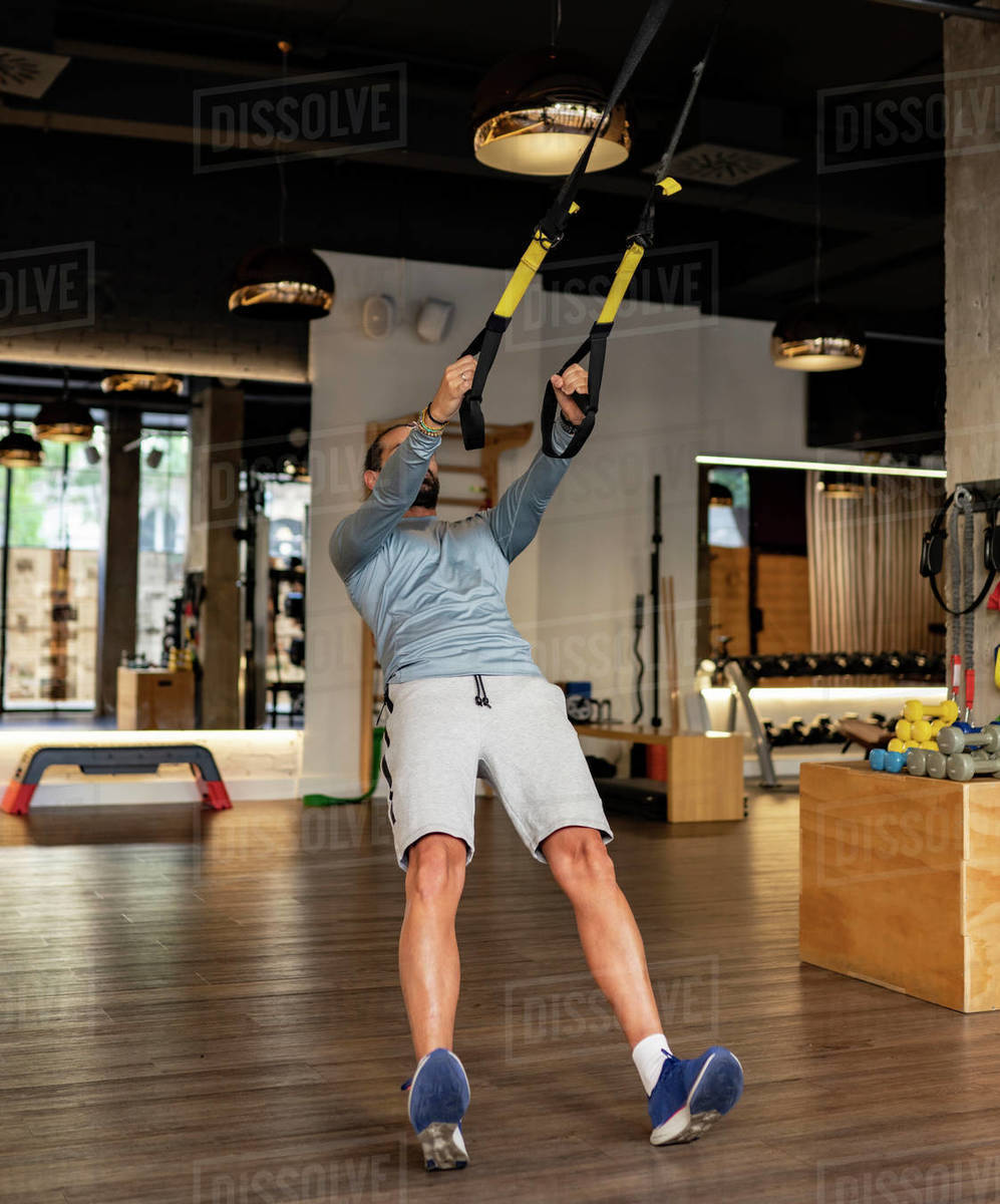 Front view of concentrated muscular male athlete practicing suspension ...