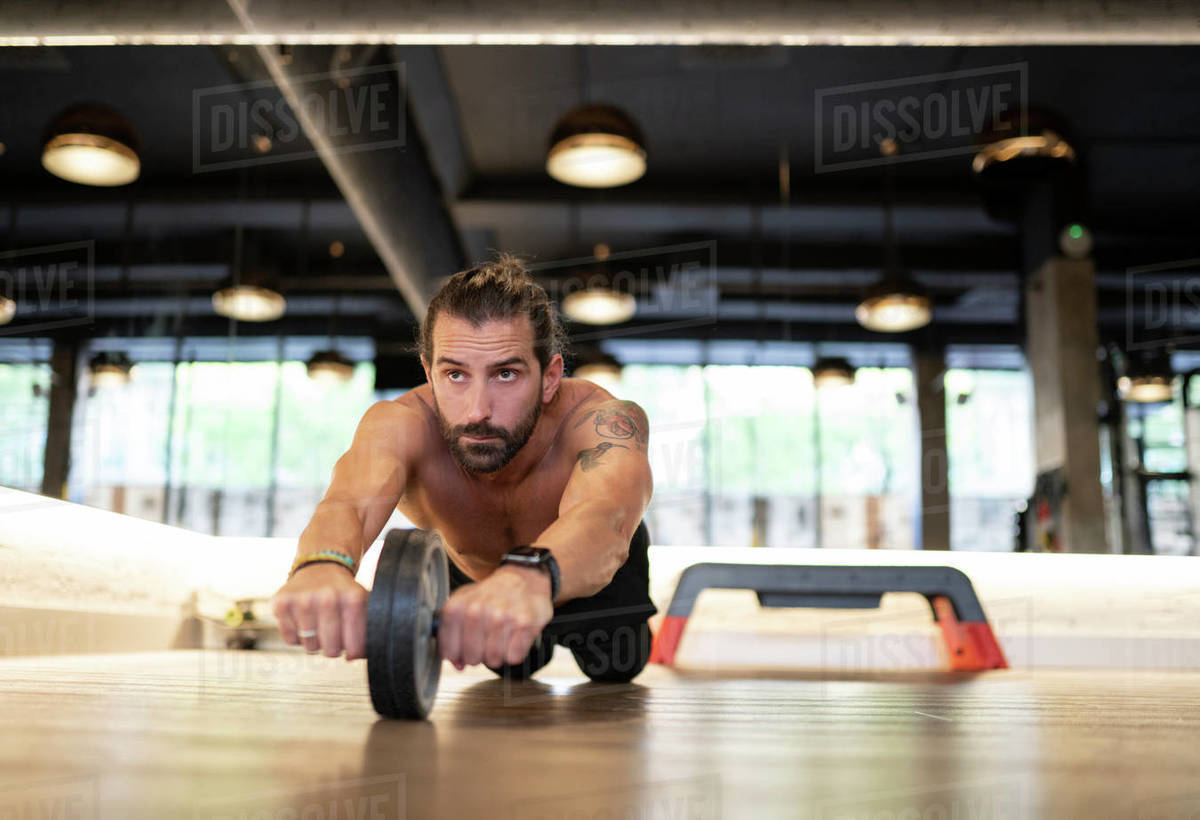 Strong bearded male athlete doing exercise with abs wheel on floor ...