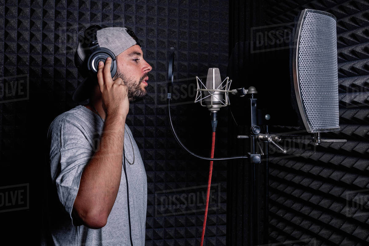 Side view of male singer in headphones and hat standing in acoustic ...
