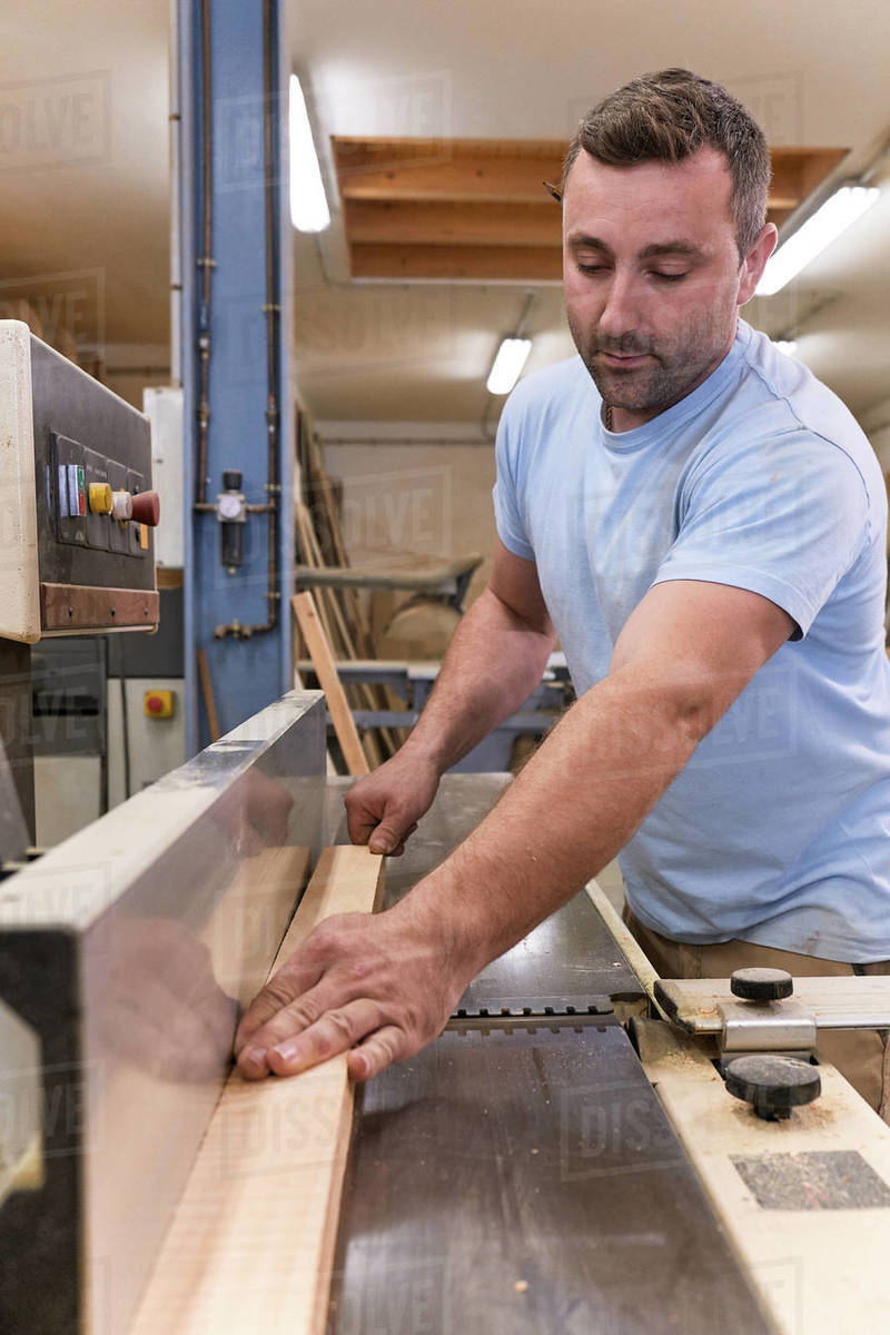 Male woodworker in casual clothes focusing and cutting lumber using ...