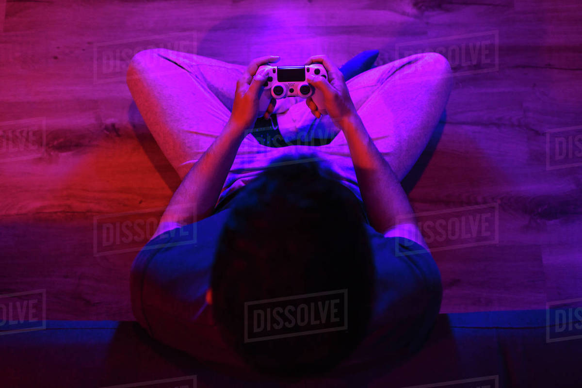 Top view of a boy sitting on the floor playing video games at night ...